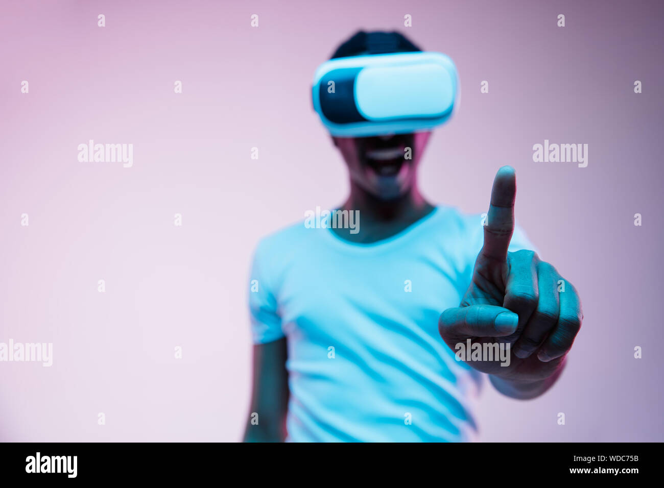 Young african-american man in VR-glasses in neon light on gradient ...