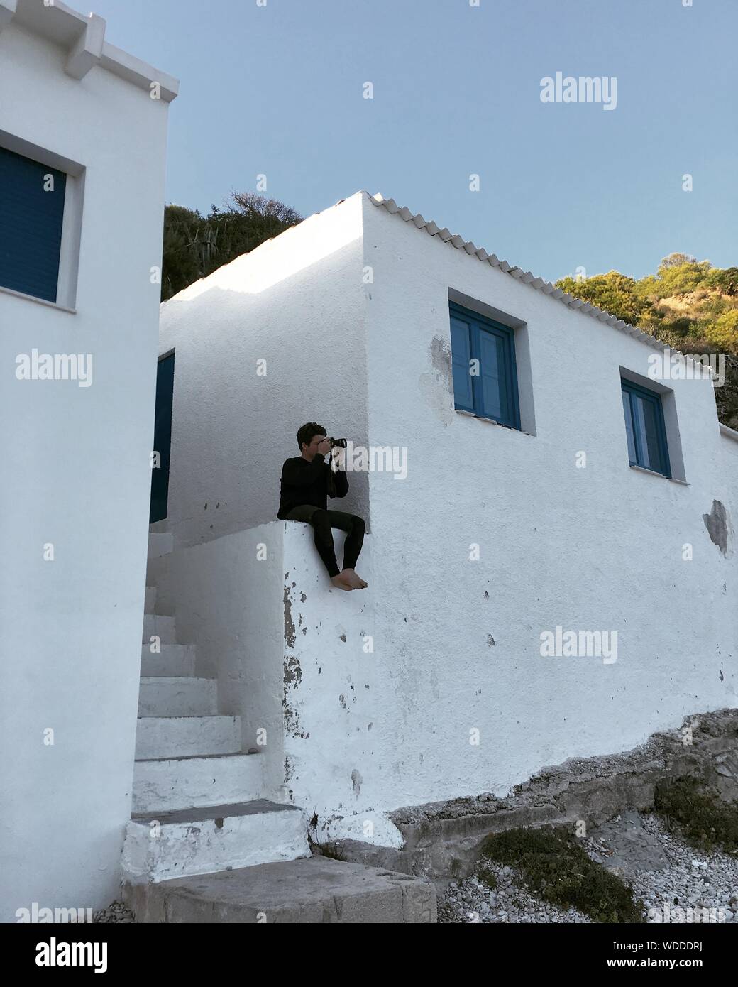 Vertical shot of a male with a photo camera sitting on the ledge of a ...