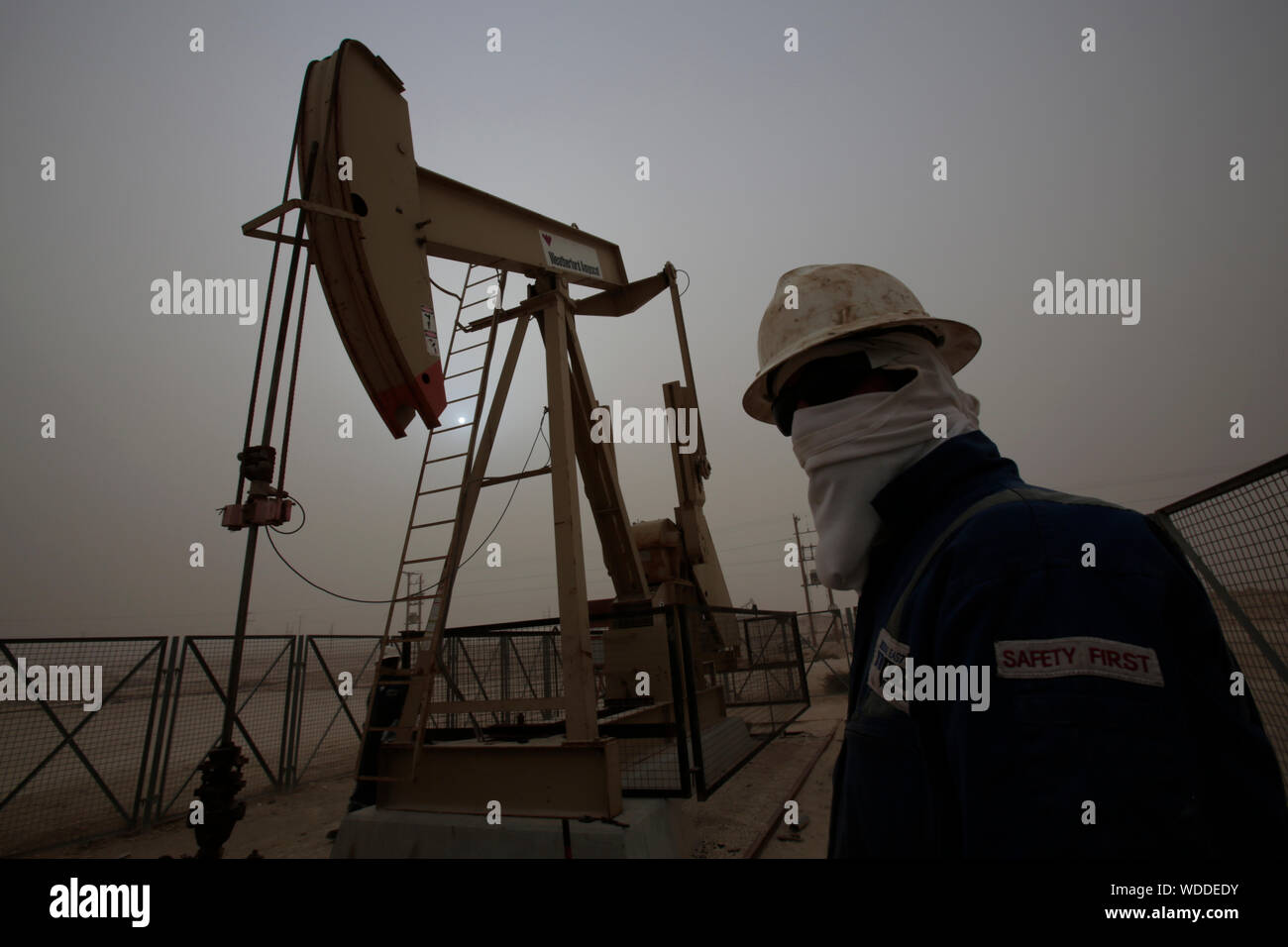 An oil worker covers his face during a sandstorm near an oil pump in ...