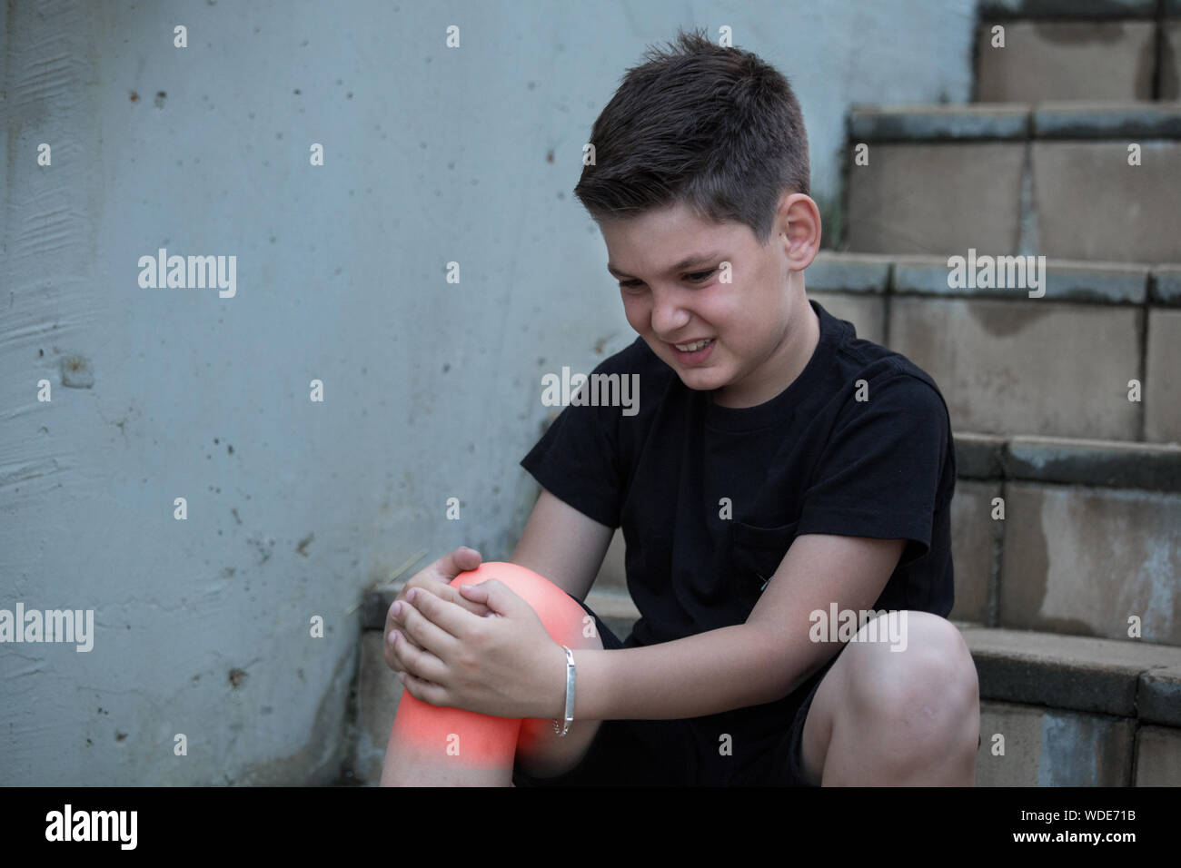 Boy in pain Looking At His Injured Leg Sitting on the stairs. Knee pain ...
