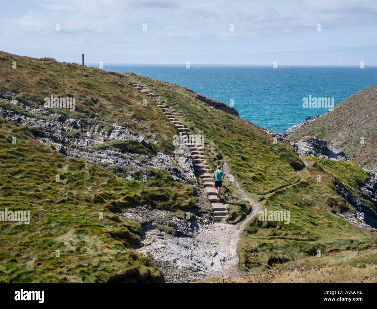 A man running up steps on the south west coast path near Porthcothan ...