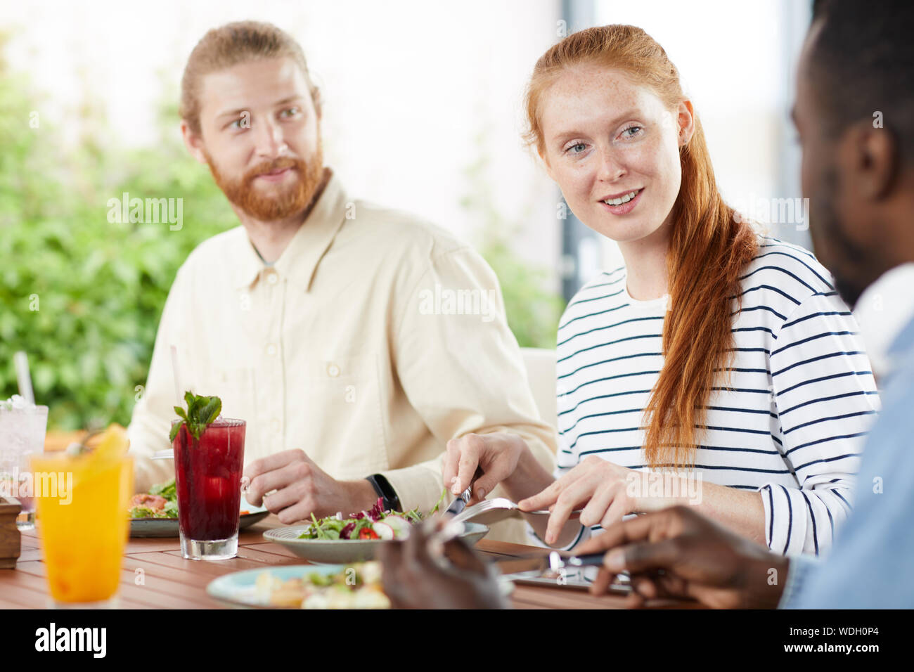 Group of young friends sitting at the table eating vegetable salad and ...
