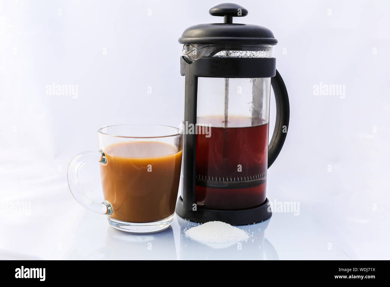 A cup of coffee in a glass mug sitting next to a cafetiere half full of ...