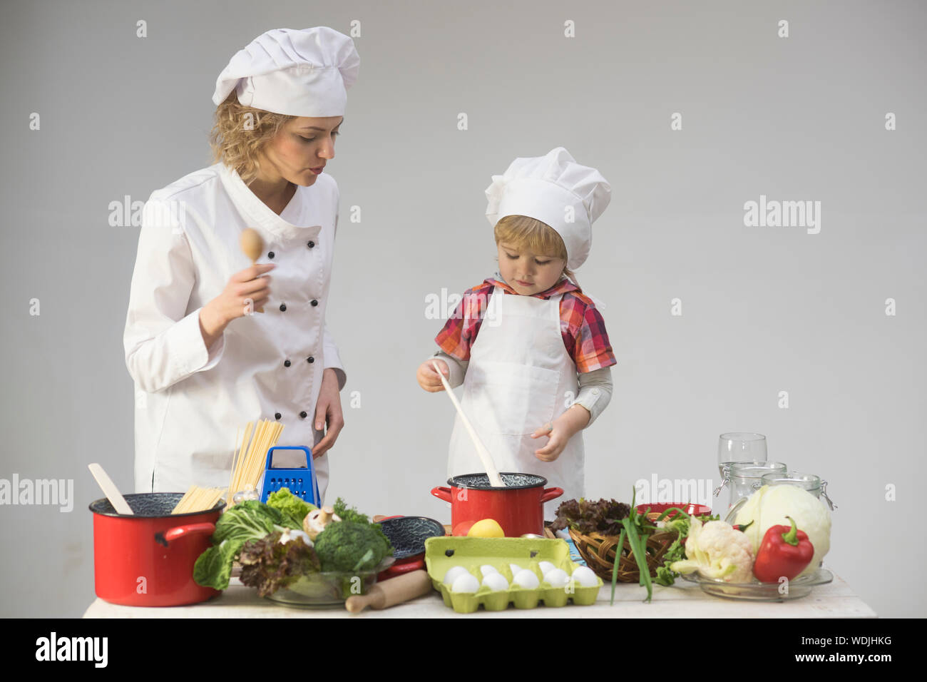 Mother teaches son to cook on light background. Chef and assistant near ...