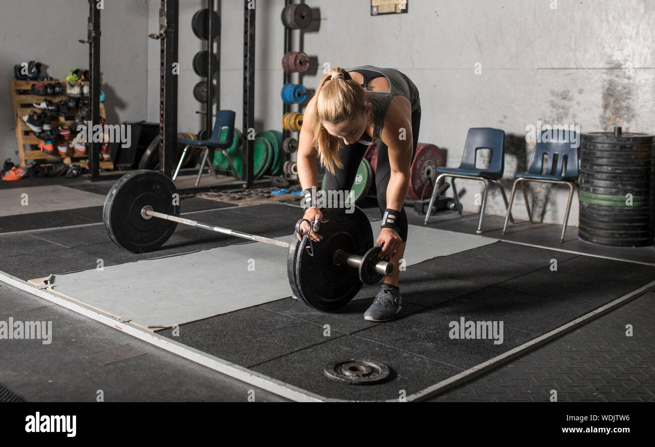 Strong young female weight lifter loading weights onto barbell in gym ...