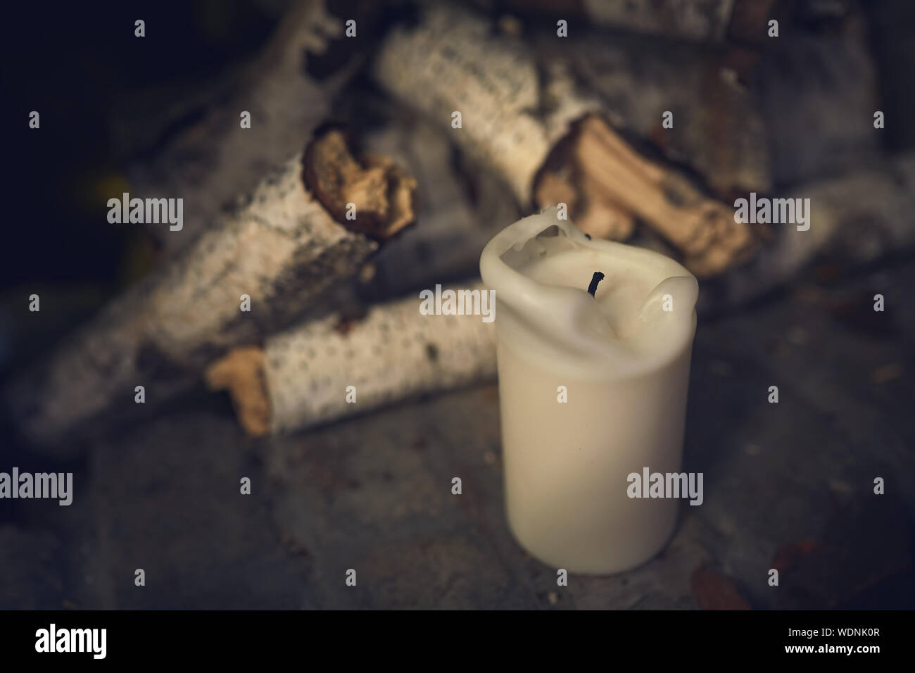 White extinct paraffin candle against a background of birch firewood ...
