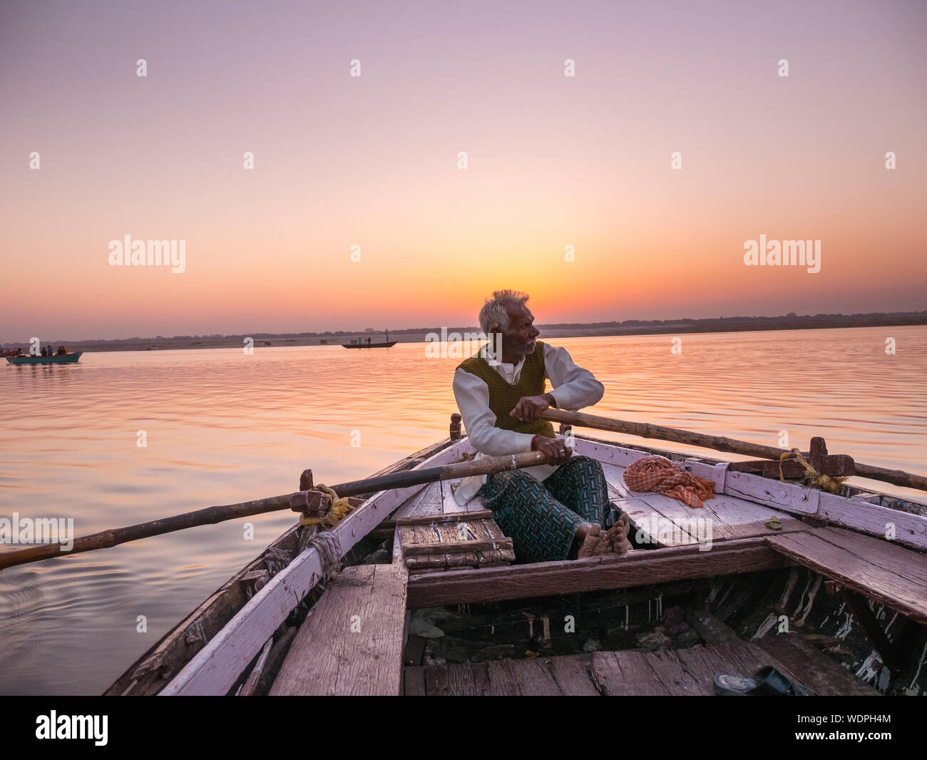 Indian man rowing a boat down the Ganges River at down in Varanasi ...