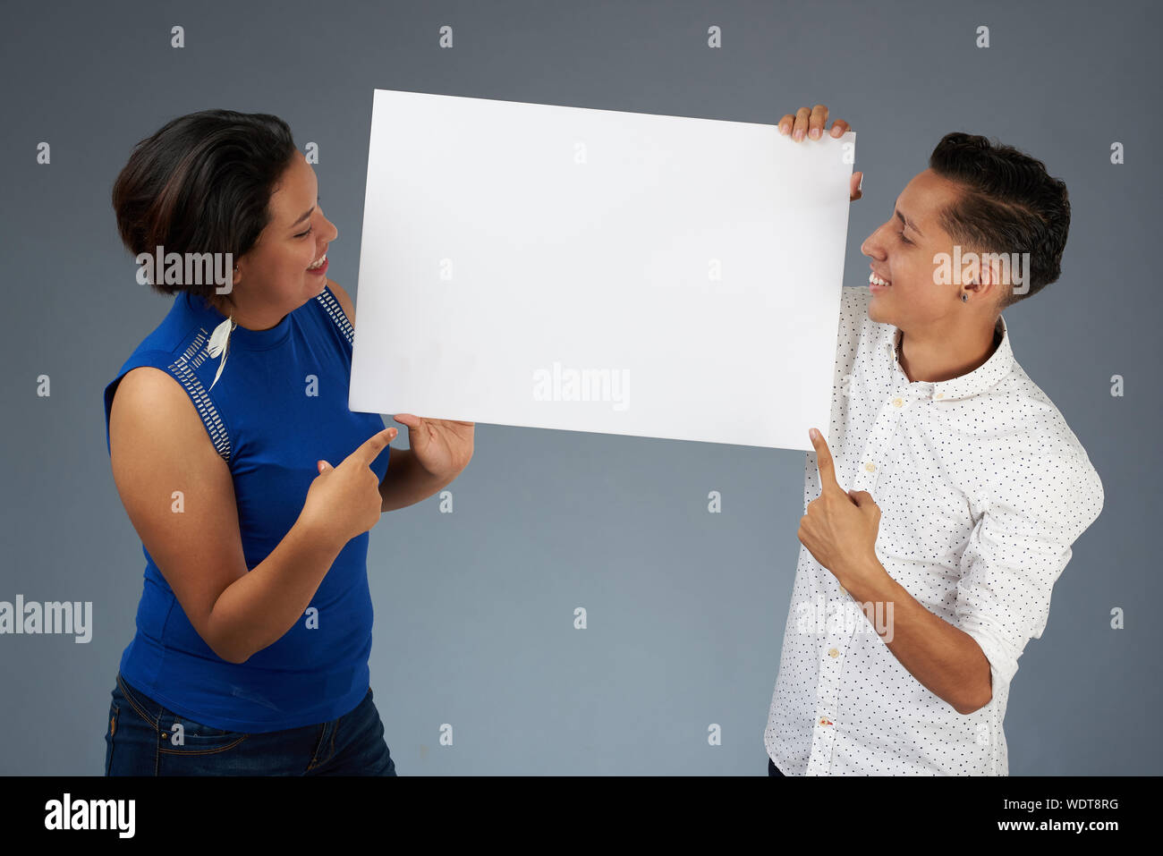 Young people point at copy space on banner isolated on gray studio ...