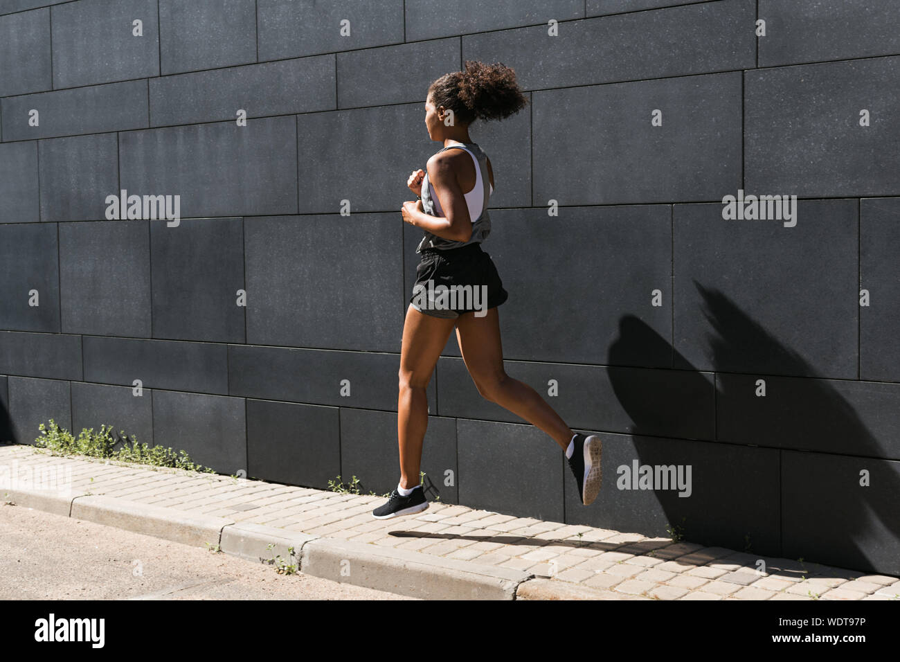 Young Woman Running On Sidewalk By Wall Stock Photo - Alamy