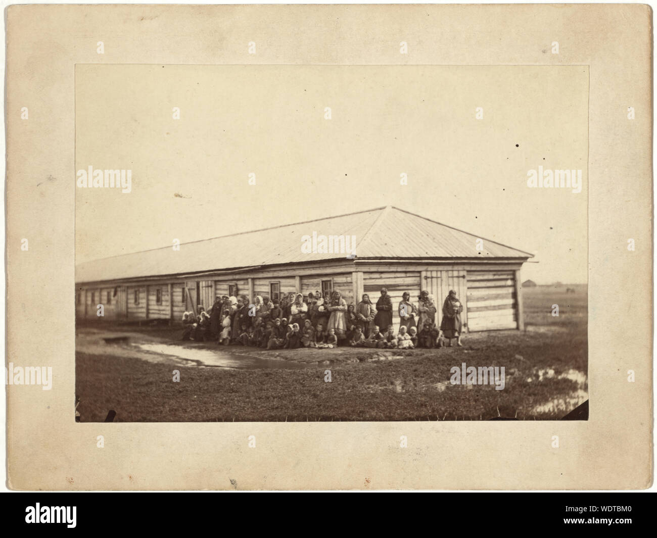 Group of female exiles and their children standing in front of log ...