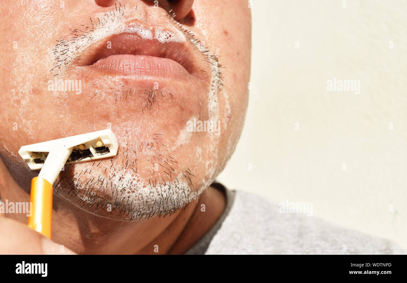 Close up the face of Asian man shaving his beard on white background ...