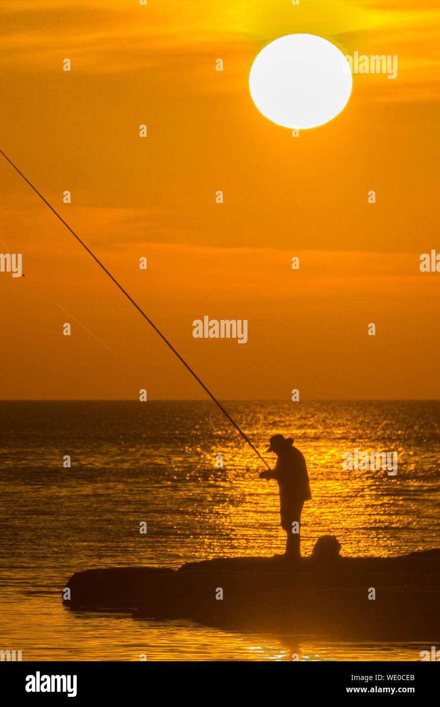 A man fishing in front of the sun in Byblos harbour in Byblos Lebanon ...