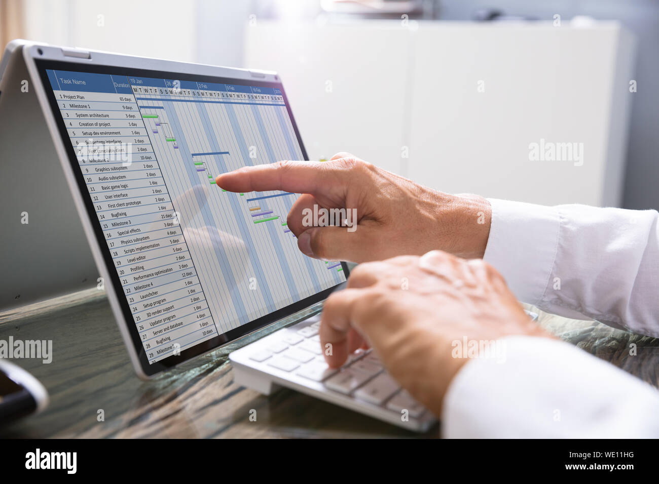 Businessman's Hand Analyzing Gantt Chart On Laptop Over Reflective Desk ...
