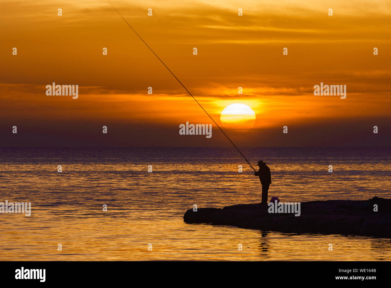 A man fishing in front of the sun in Byblos harbour in Byblos Lebanon ...