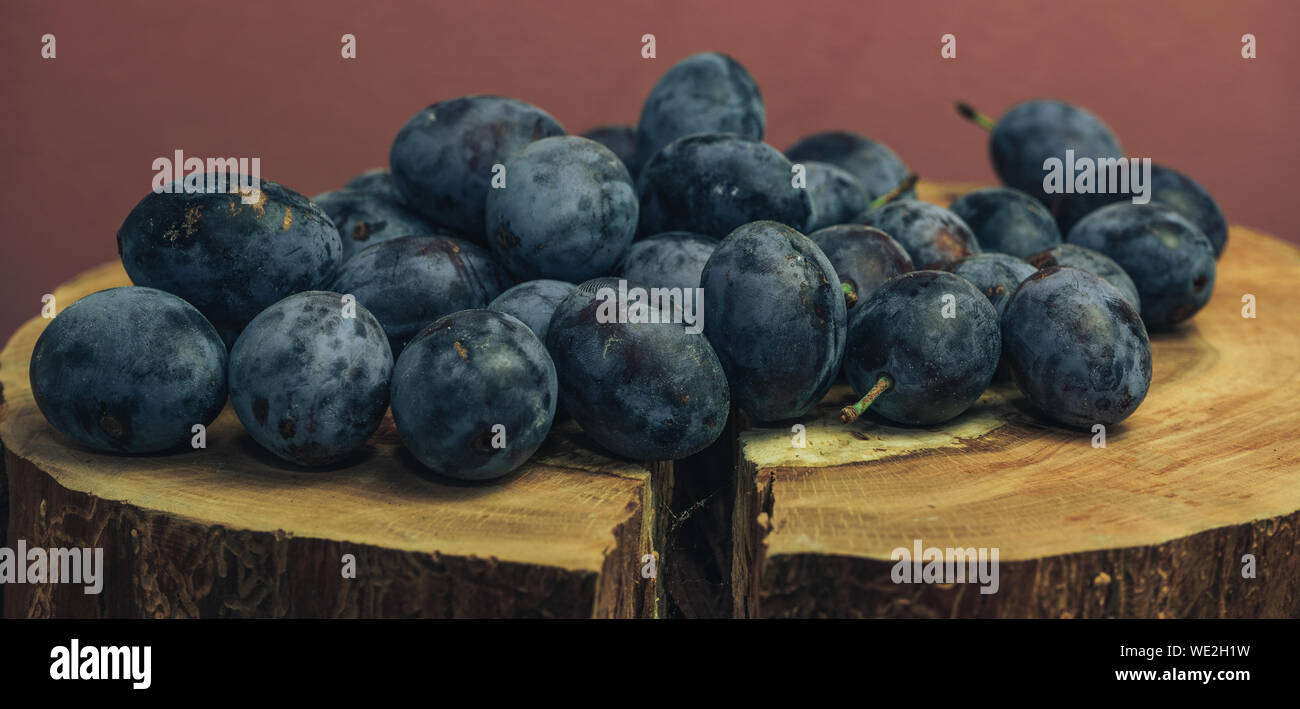 Beautiful fresh blue plums on a tree stump and red wall background ...