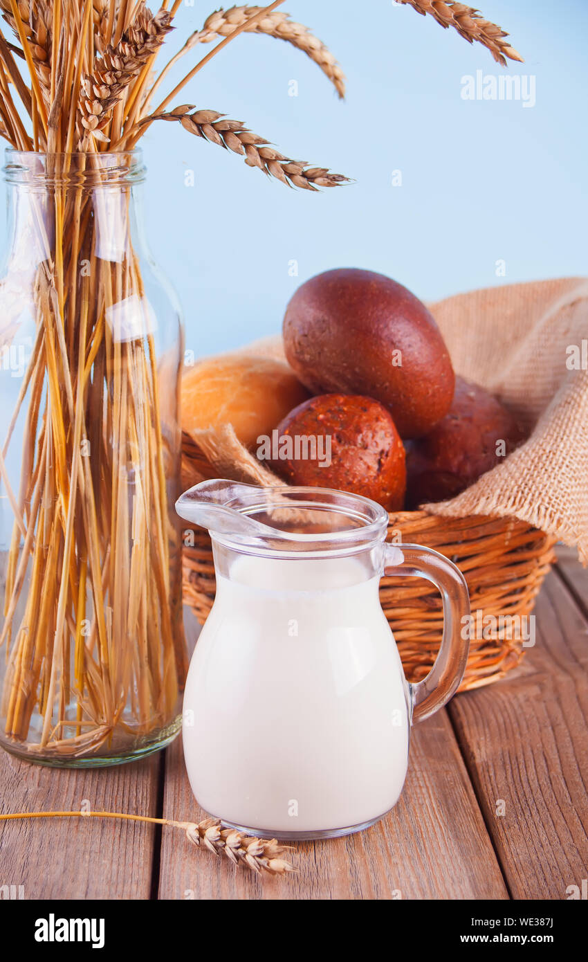 Vase with a bouquet of wheat stems, jar of milk and basket with bread ...