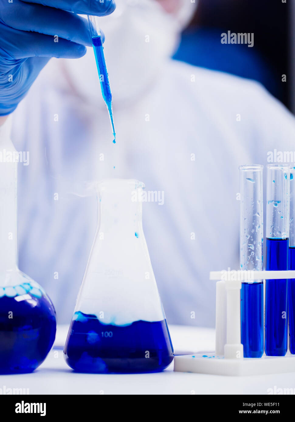 Scientist in a research laboratory taking a sample of blue solution ...