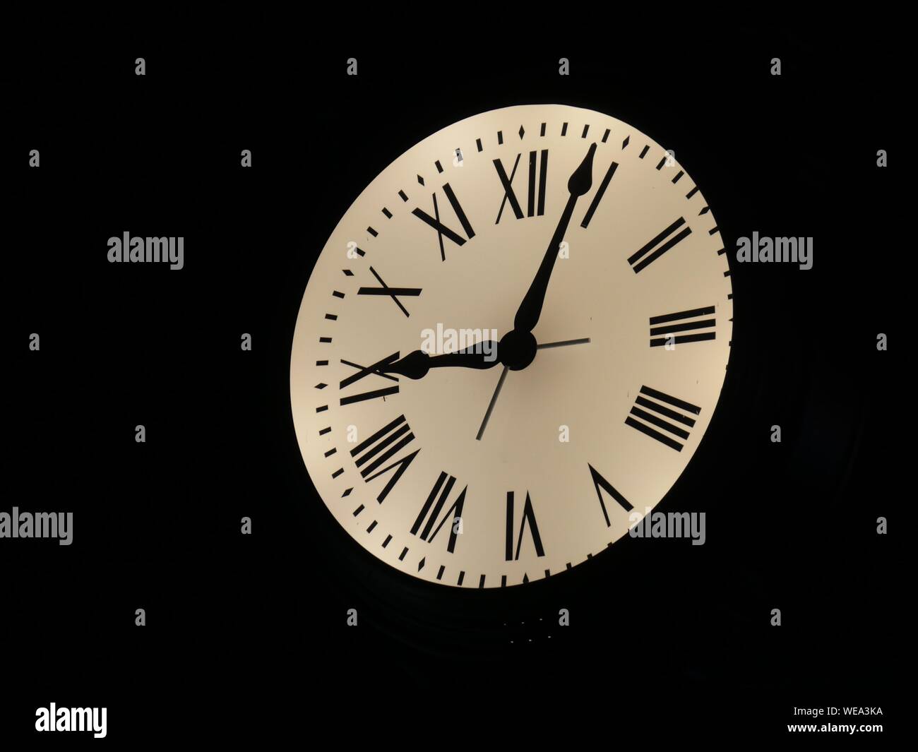 Wall clock with Roman numerals, black background Stock Photo - Alamy