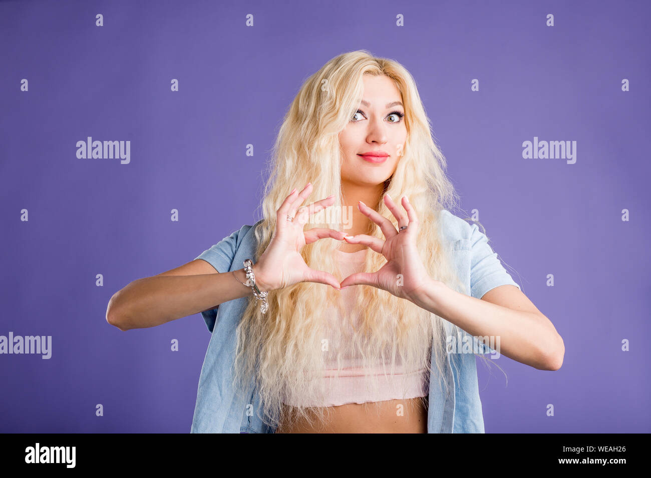 Tender romantic blonde young woman making heart shape by hand over ...