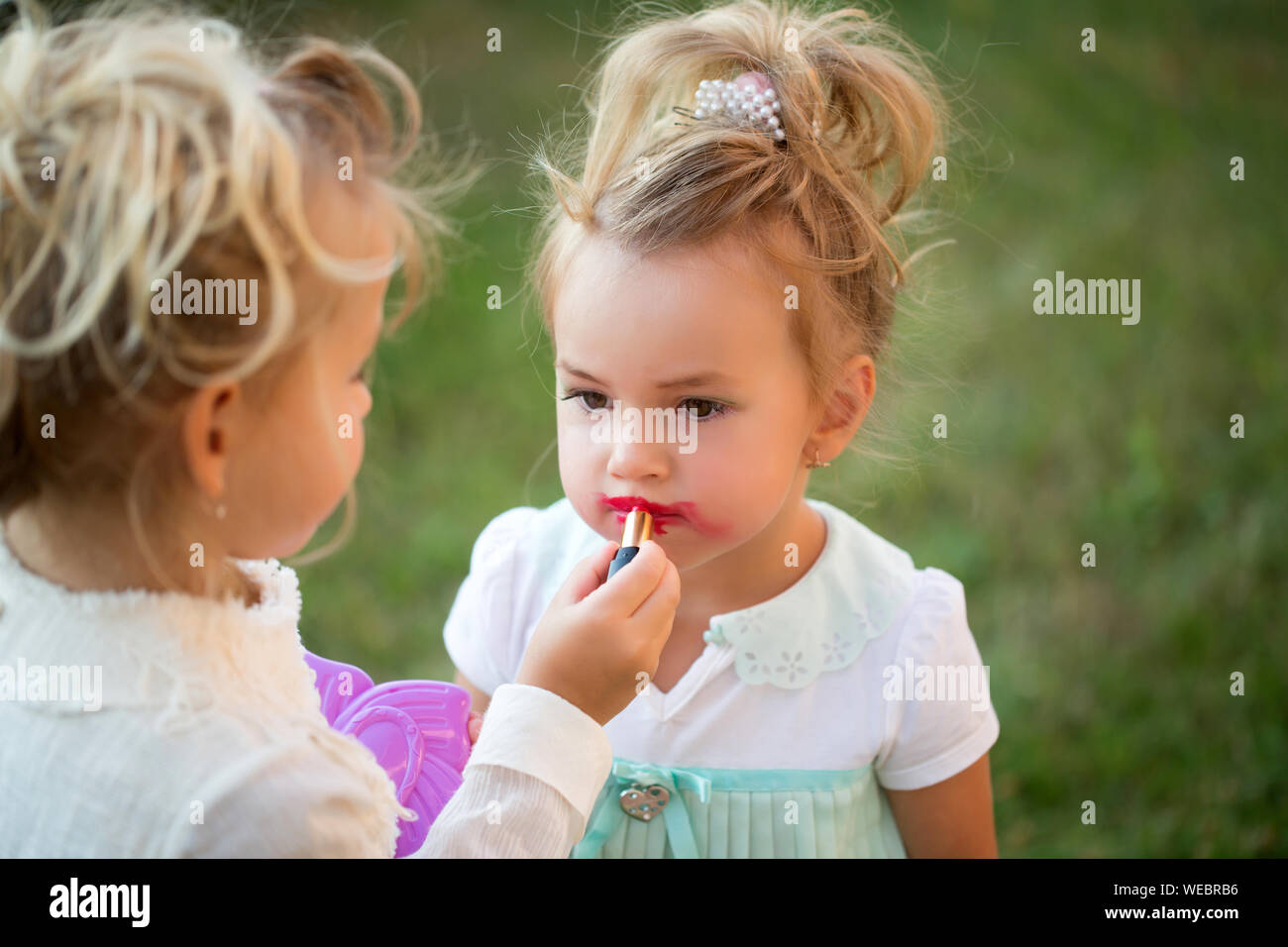 Baby apply red lipstick on lips of kid model. Girl do makeup for sister ...