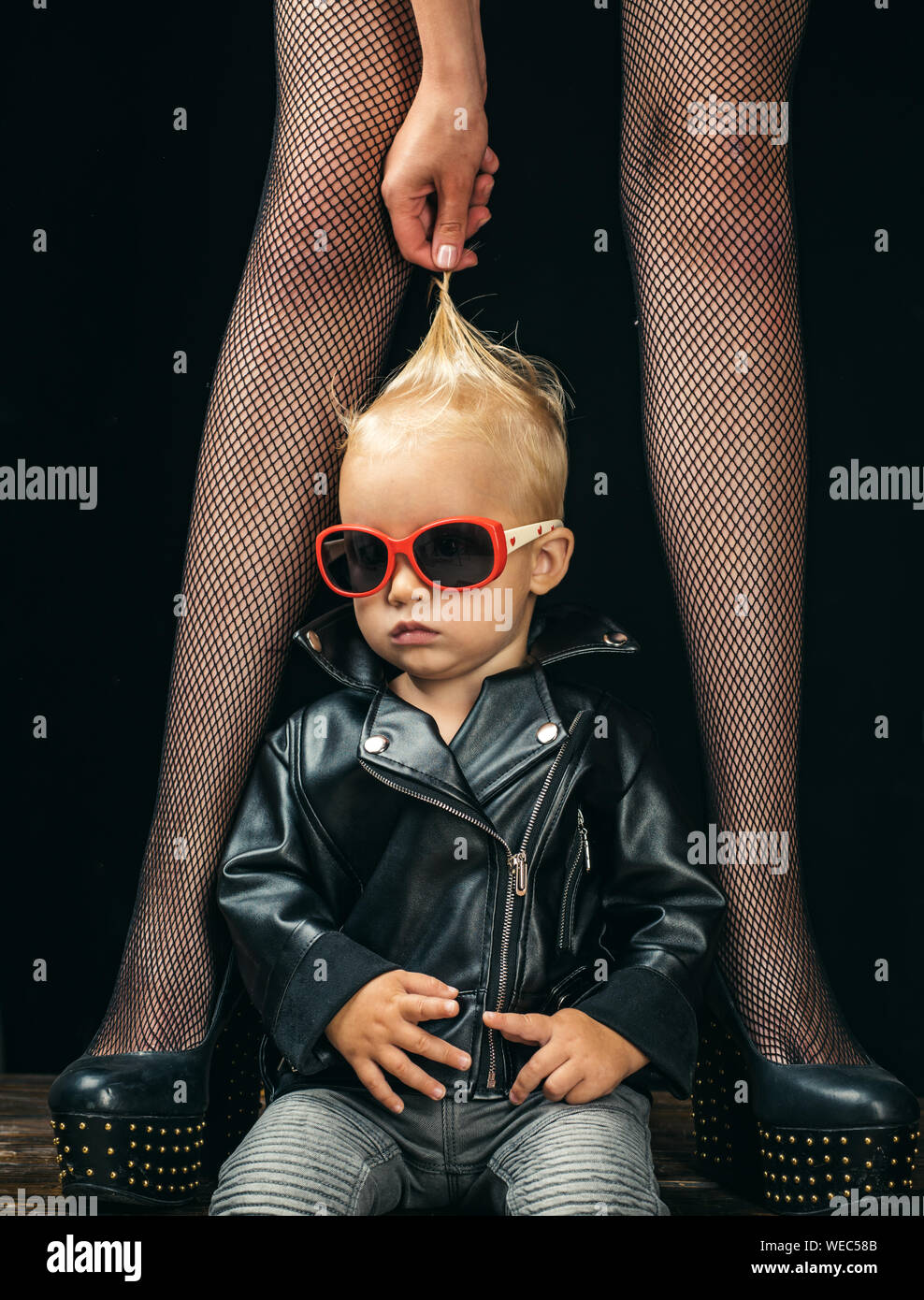 Forever rocker. Rock and roll fashion trend. Small boy at female legs ...