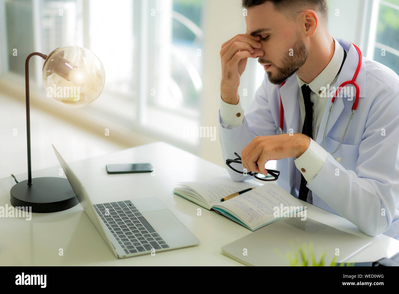 Stressed doctor sitting at his desk in his office while he overworke at ...