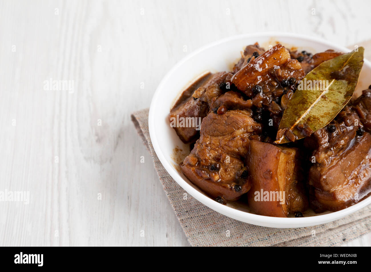 Homemade Filipino Adobo Pork in a bowl on a white wooden surface, side ...