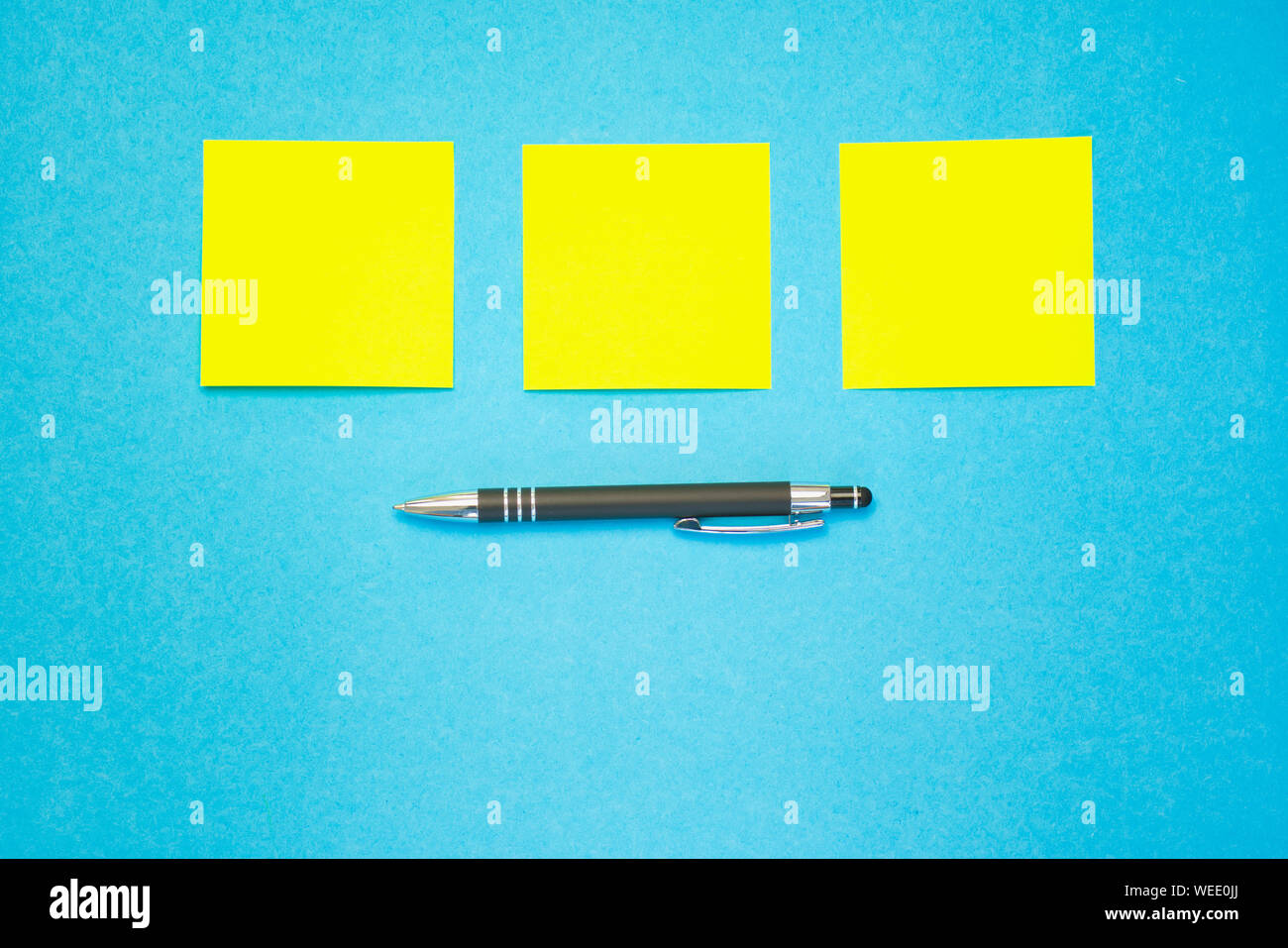 three yellow adhesive labels in a row over a pen against blue ...