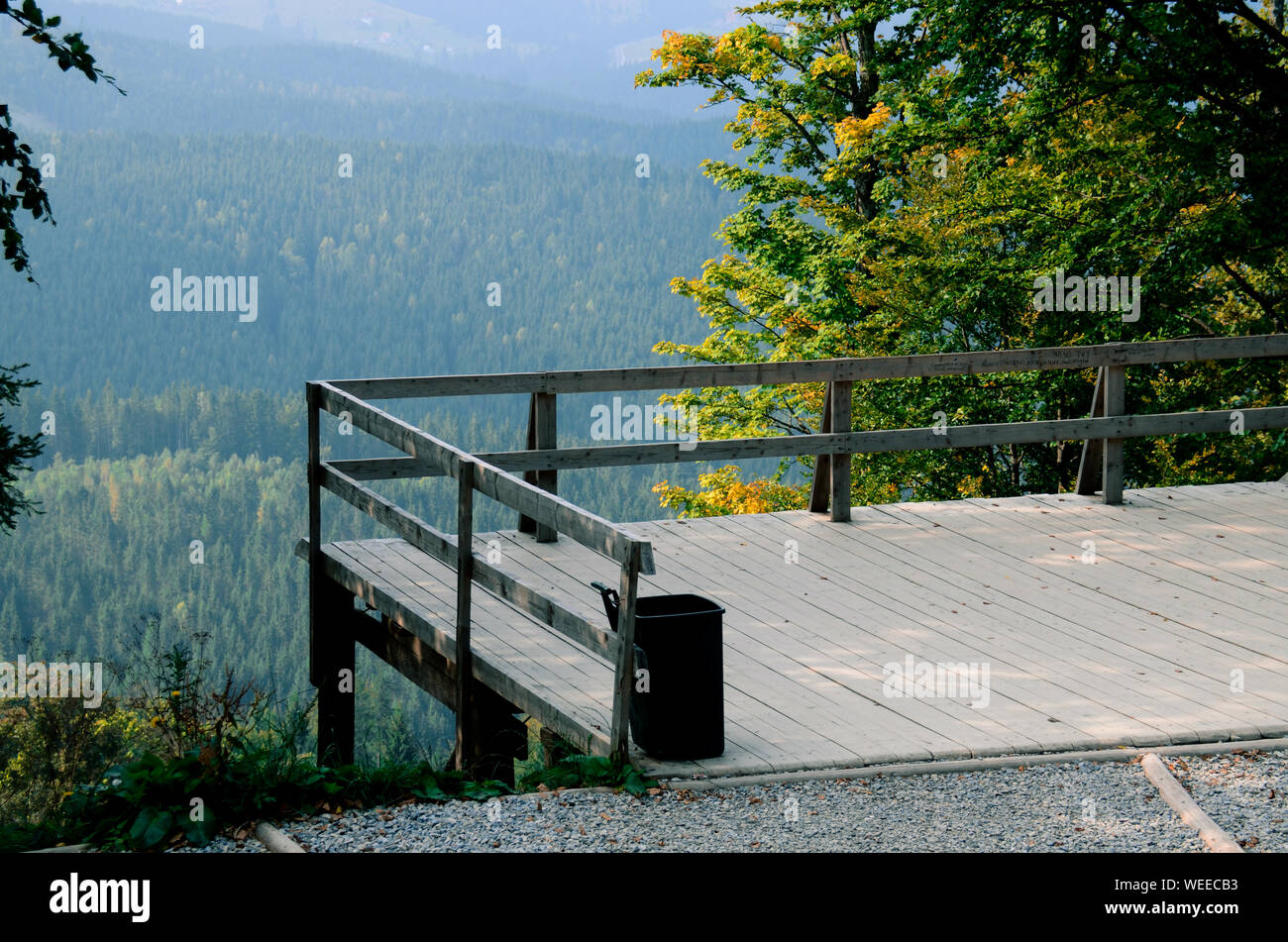 A wooden observation deck over a cliff overlooking the mountain slopes ...