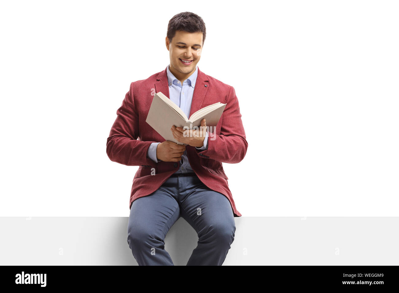 Young man sitting on a panel and reading a book isolated on white ...