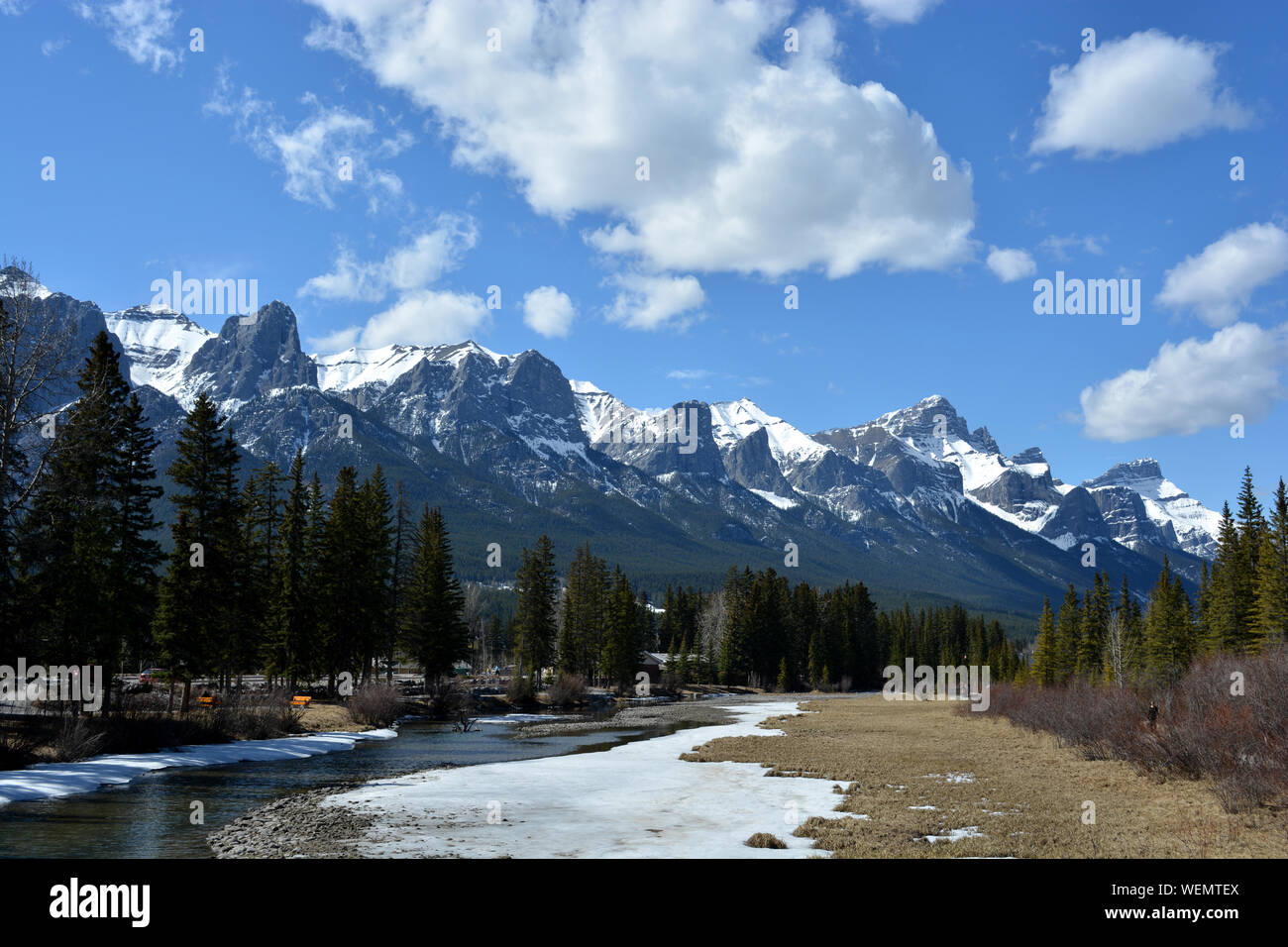 Tree-lined stream with snow and mountain range Stock Photo - Alamy