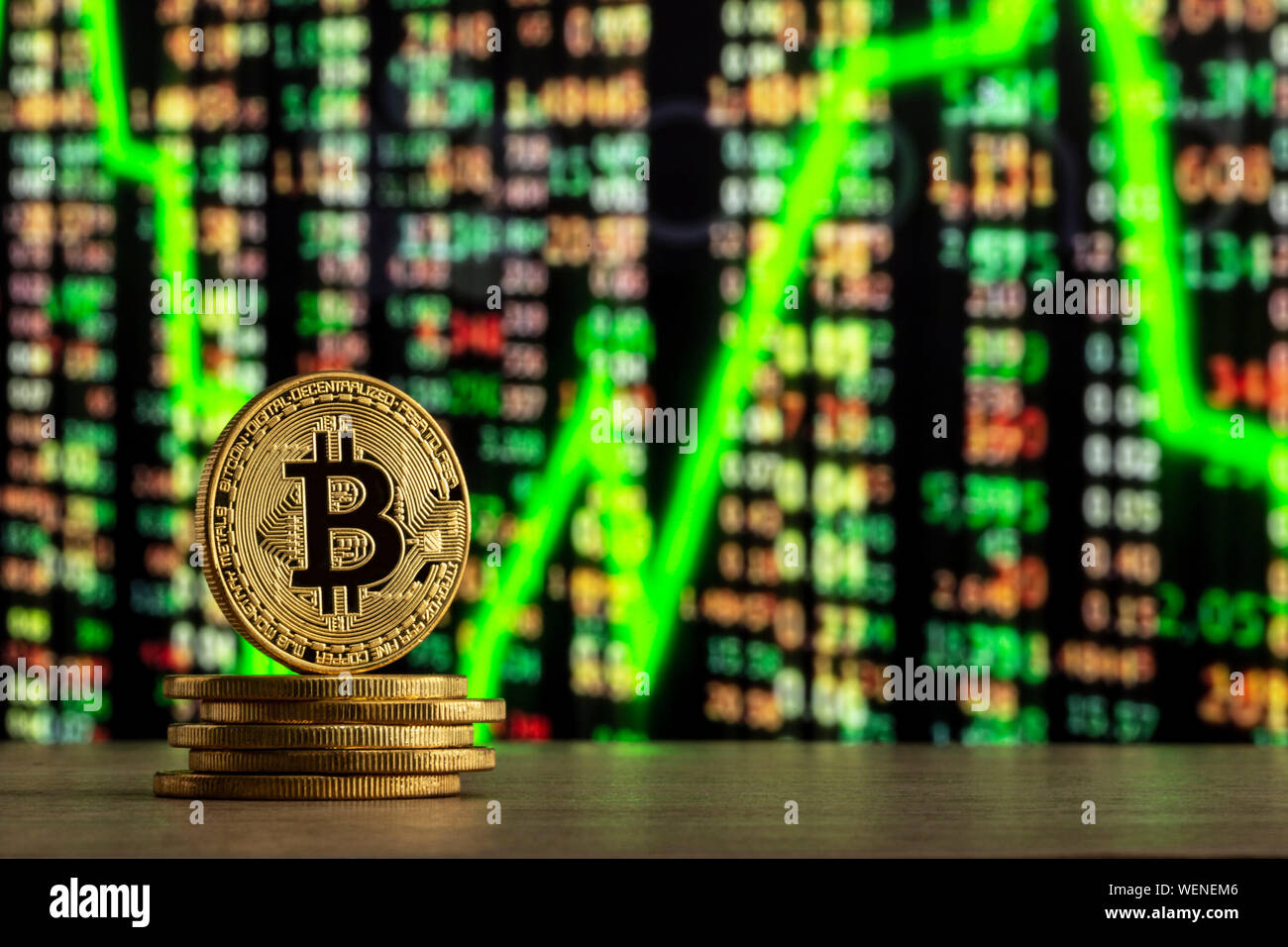 physical bitcoin standing at a wood table in front of a numbers graph ...