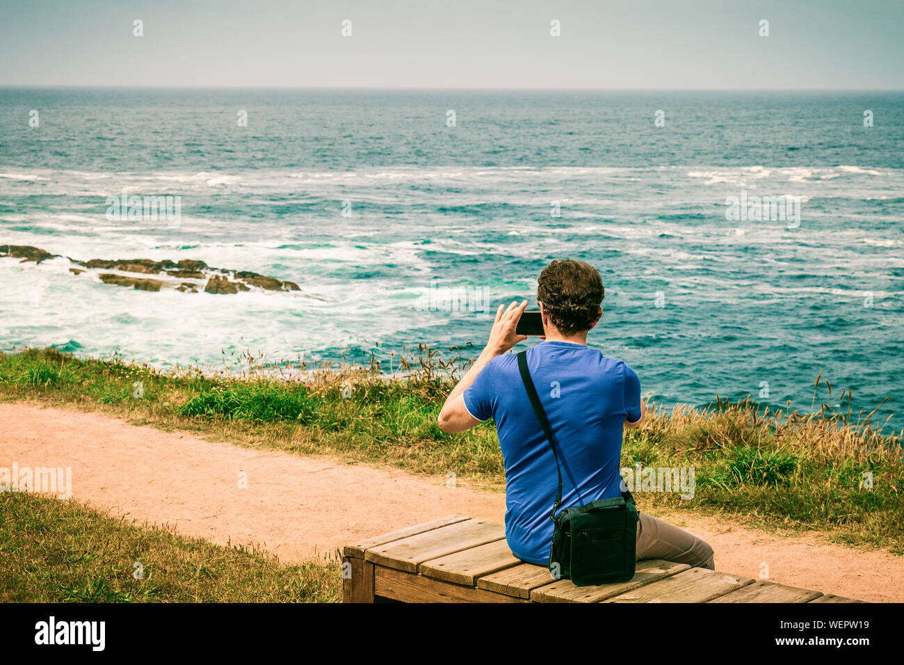 tourist sitting io a bench facing the sea with mobile phone taking ...