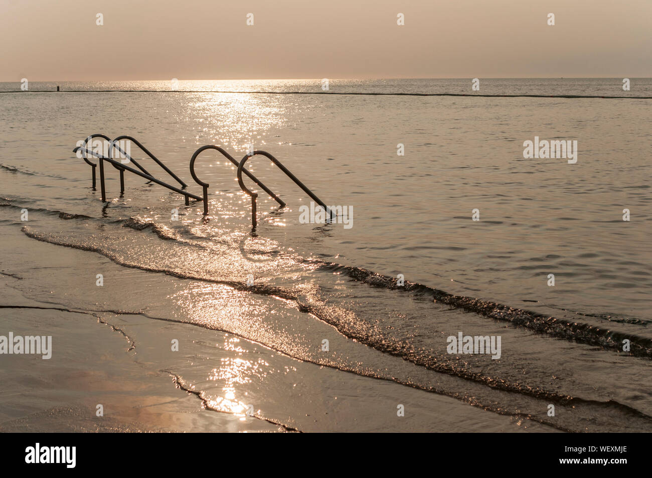 Sunset at the empty beach. Waves and ladders on a pier Stock Photo - Alamy