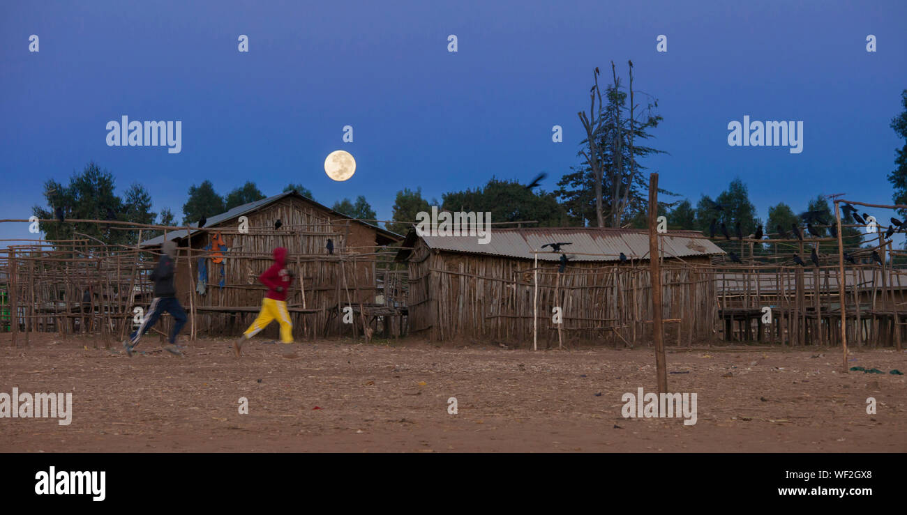 People run through an African village at night with the moon in the sky ...