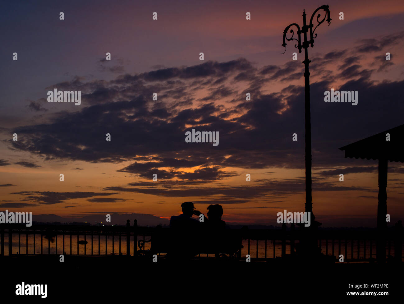 Silhouette of two people watching the sunset from a bench at Dal Lake ...