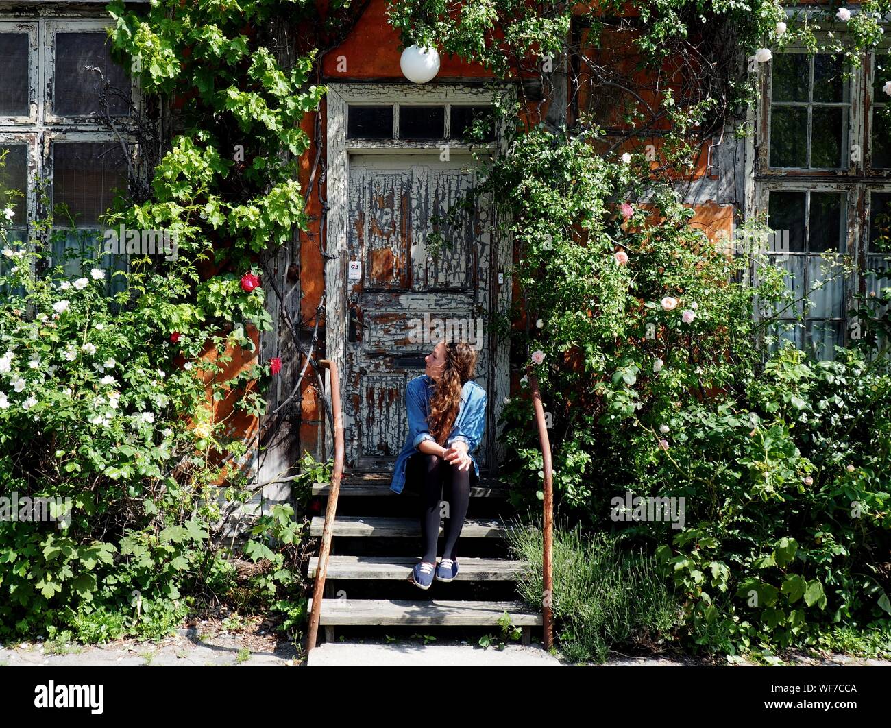 Young Woman Sitting On Front Stoop Amidst Plants Stock Photo - Alamy