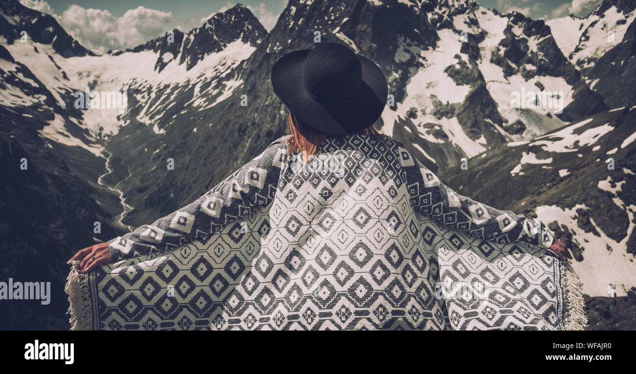 Boho woman wearing hat and poncho standing by the mountain. Cold ...