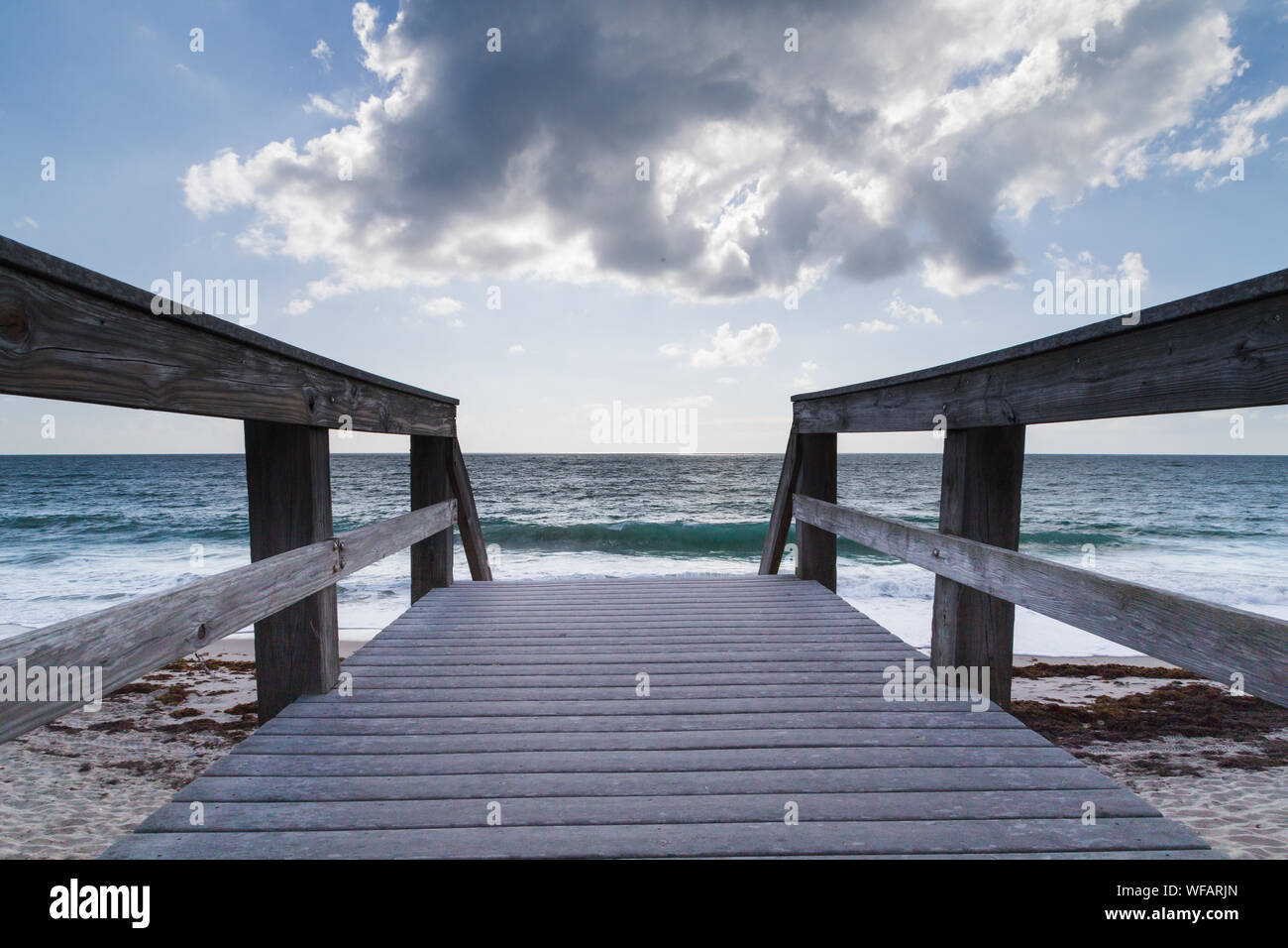 Wooden deck leading to the beach front with a large cloud overhead ...