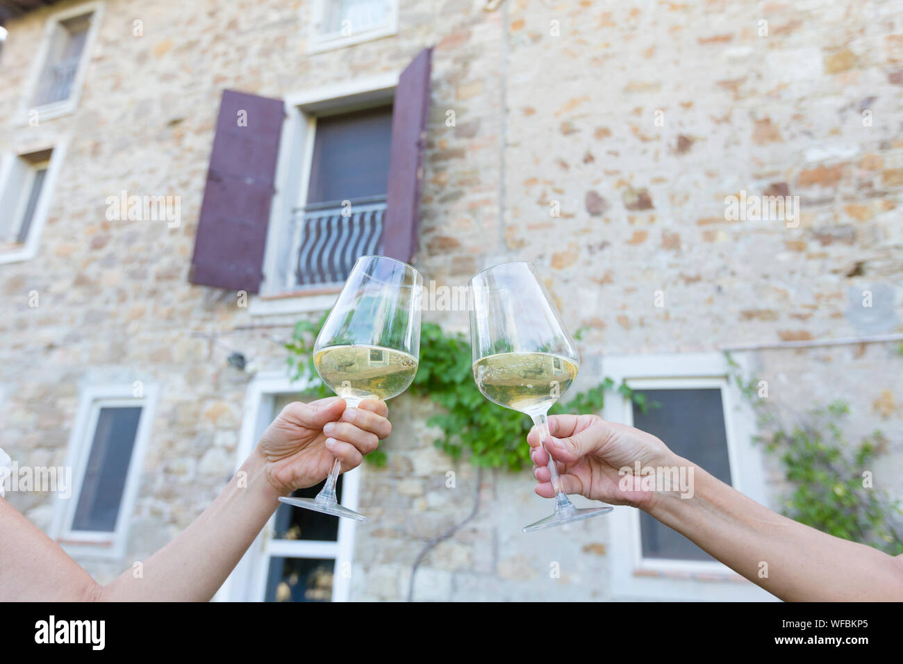 Couple drinking a toast with white wine in front of an old house, Italy ...