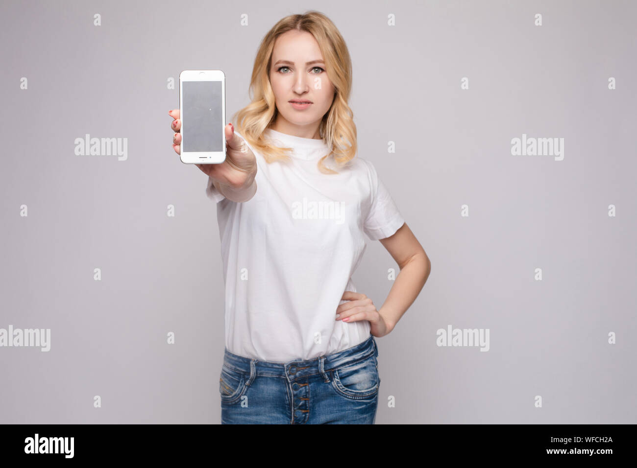 Pretty girl pointing at cell phone.Studio portrait of beautiful ...