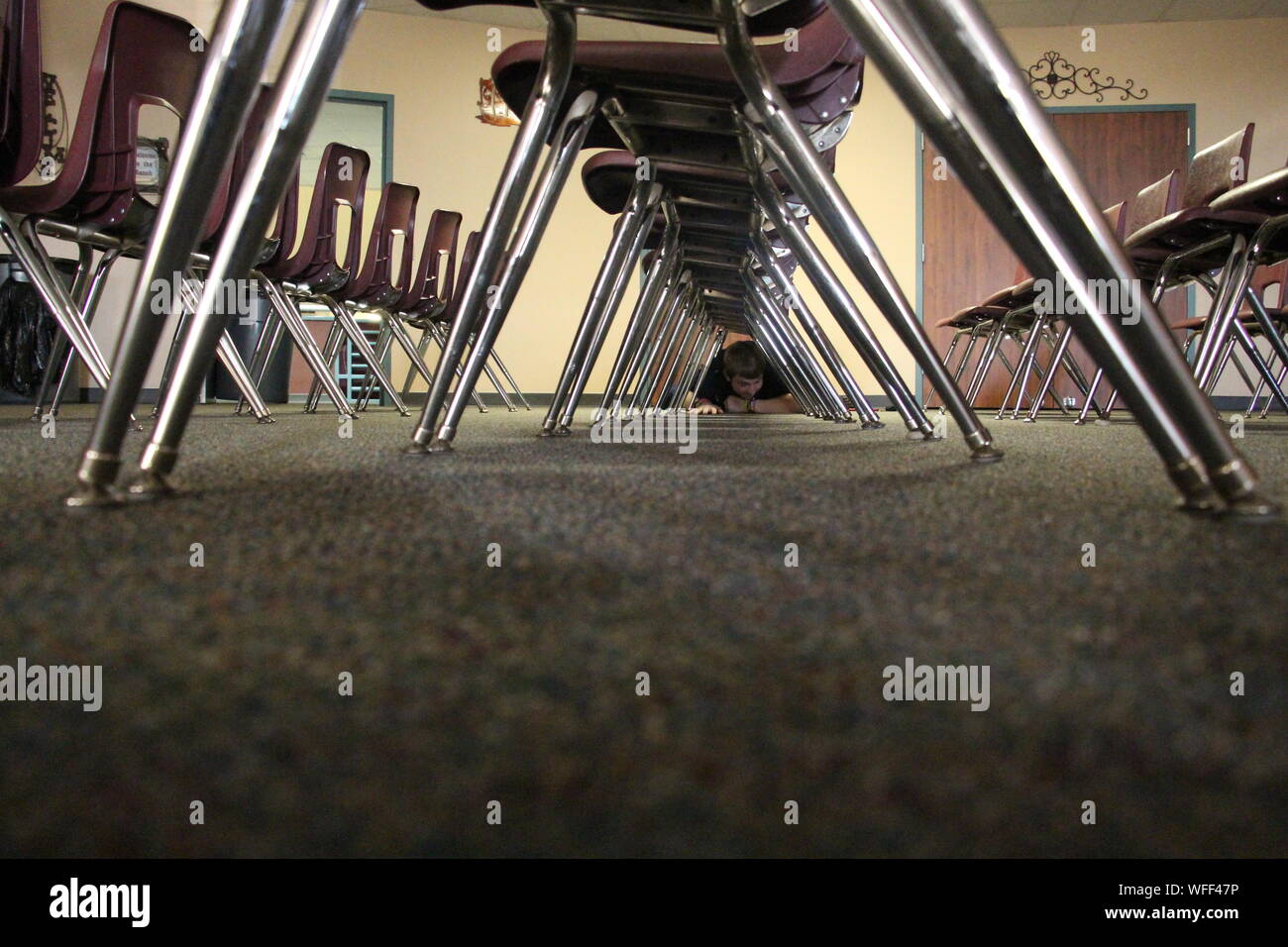 Boy Hiding Under Chairs In Room Stock Photo - Alamy