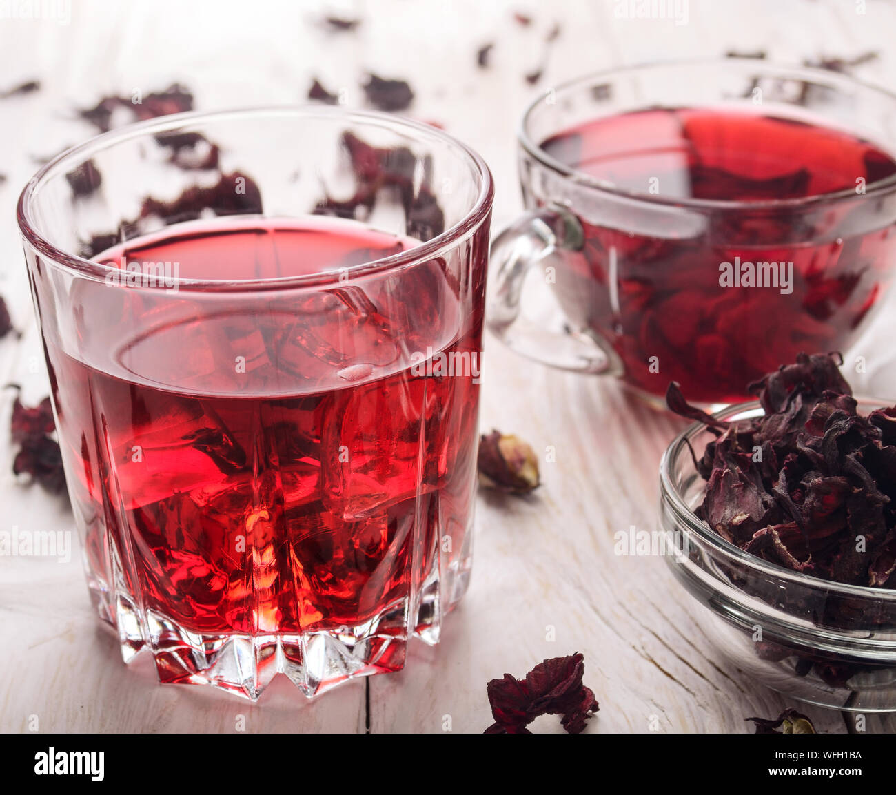 Closeup view at two tea cups with ice and dry hibiscus petals on white wooden table background ...