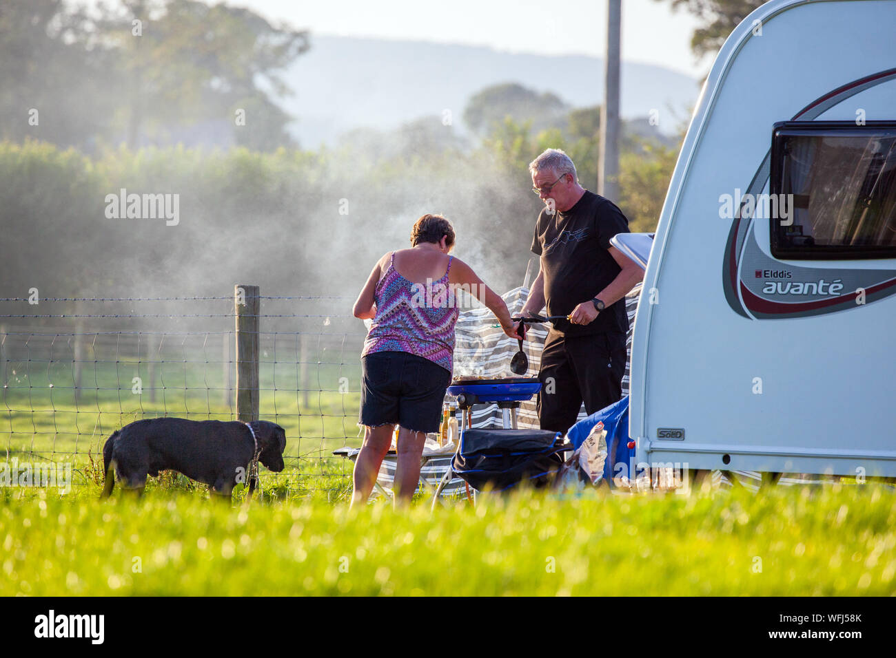 Man and woman couple cooking on a BBQ outside their touring caravan in ...