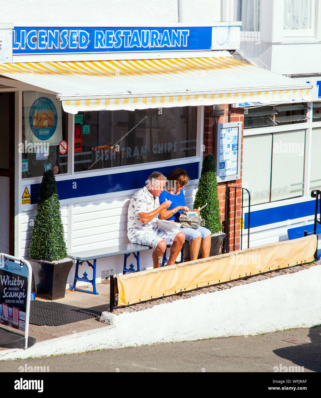 Man and woman couple people eating sitting outside a fish and chip shop ...