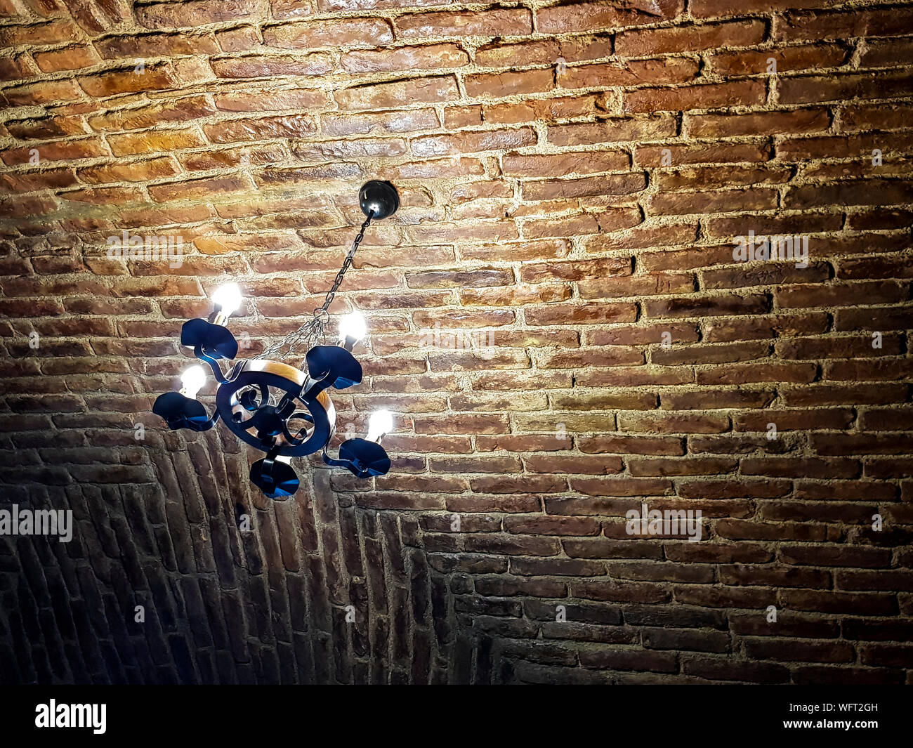 Antique chandelier style with modern lights. It hangs on a red brick ...
