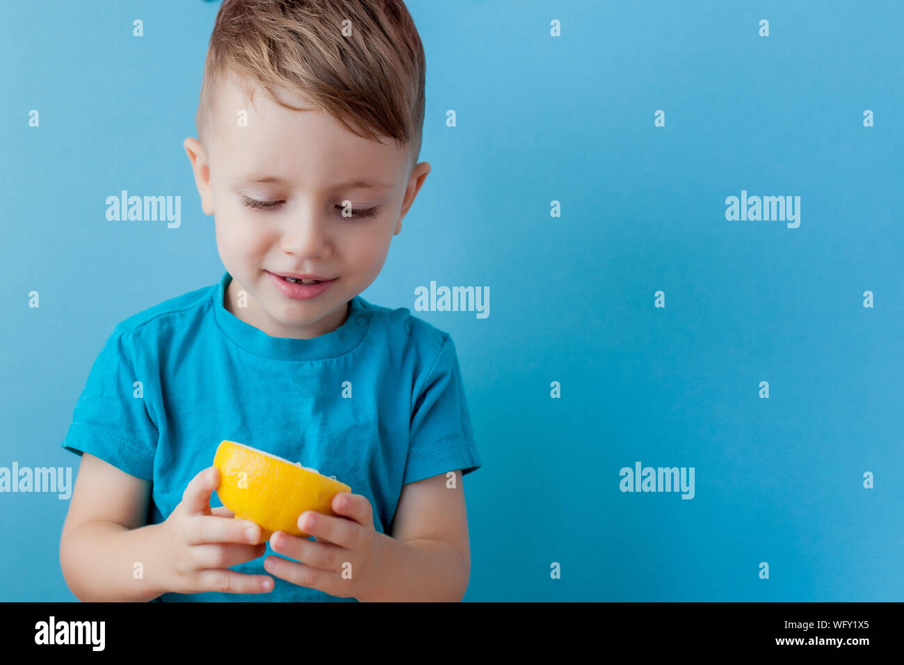 Little, blond boy biting into a lemon and make a face Stock Photo - Alamy
