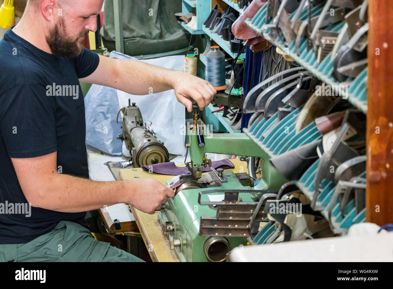 Male shoemaker skiving leather with a vintage skiving machine, working ...