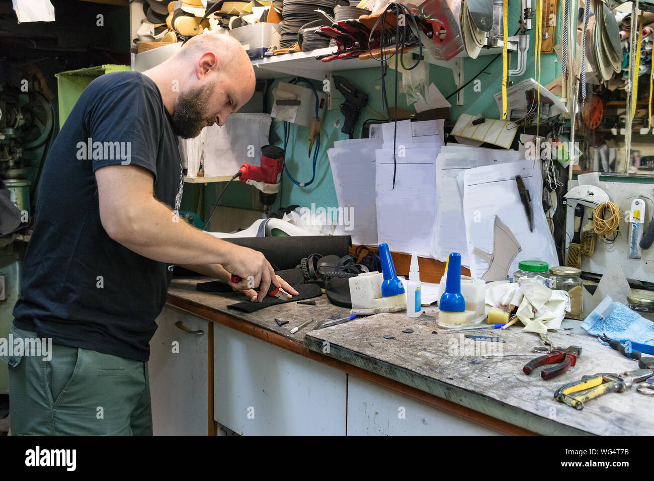 A male shoemaker cutting with a cutter on a rubber sole to repair a ...