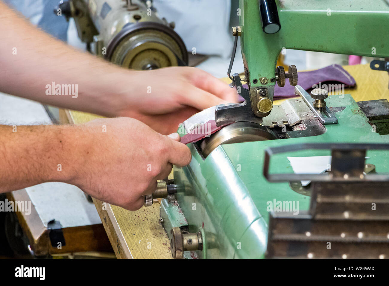 Male shoemaker hands skiving leather with a vintage skiving machine ...